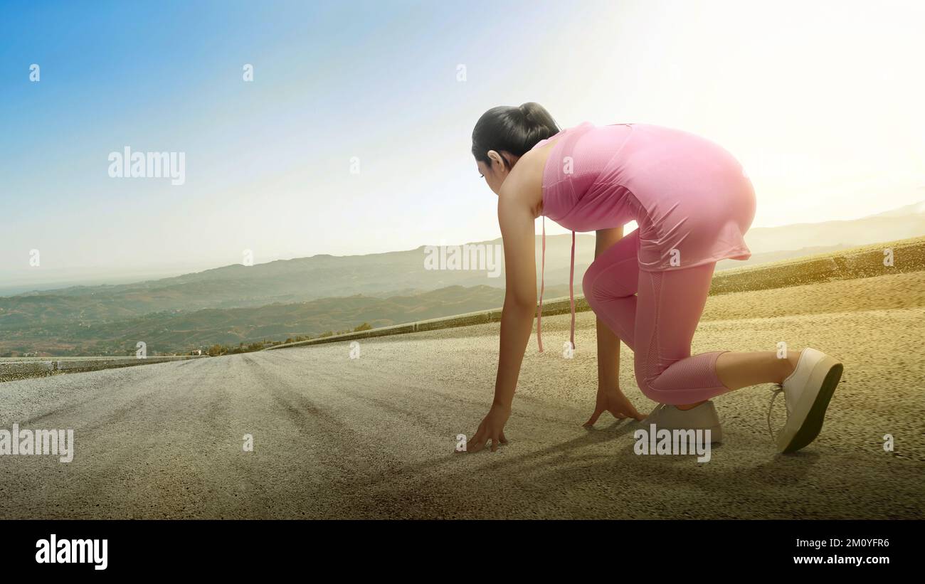 Rear view of an Asian woman in the start position ready to run on the ...