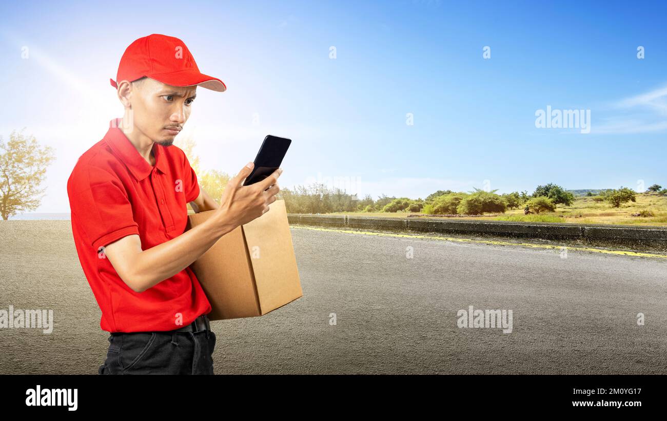 Parcel delivery man with a hat holding a mobile phone while carrying a ...