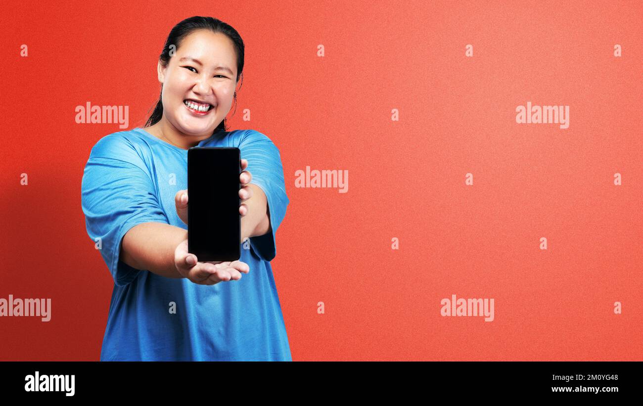 Asian fat overweight woman holding a mobile phone and showing an empty ...