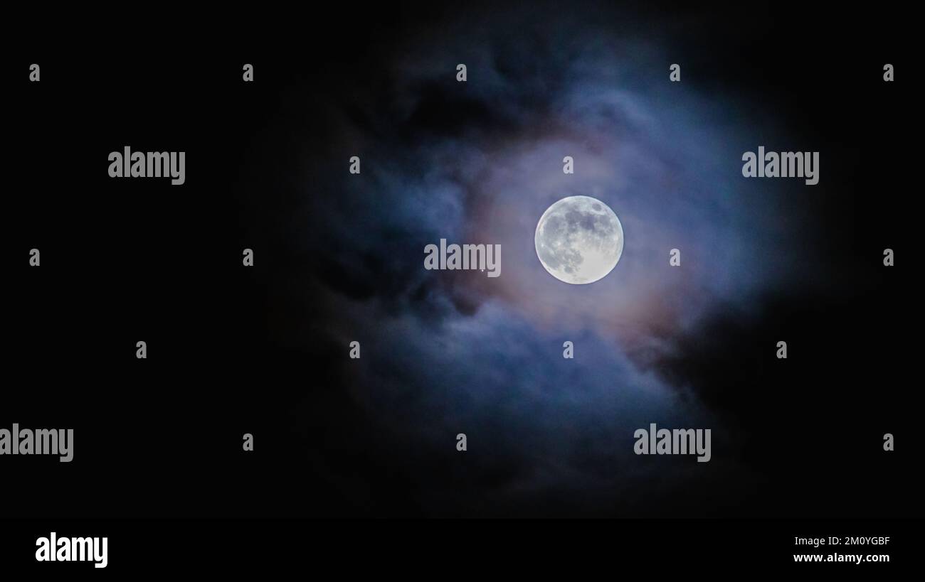 A celestial shot of the full moon through a break in the clouds with ...