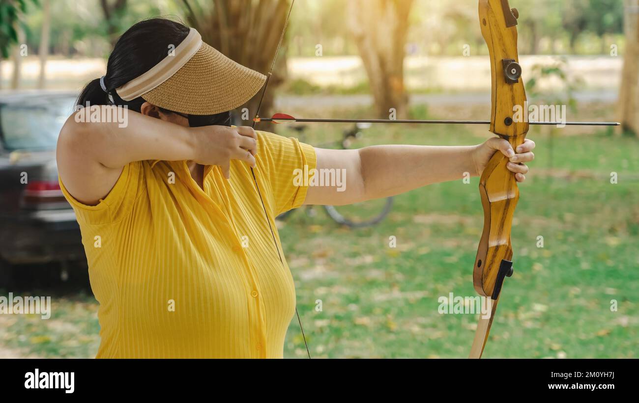 Asian woman wear visor with face mask aims archery bow and arrow to ...
