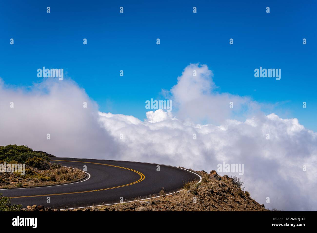 Curved paved mountain road high above fluffy white clouds in Haleakala ...