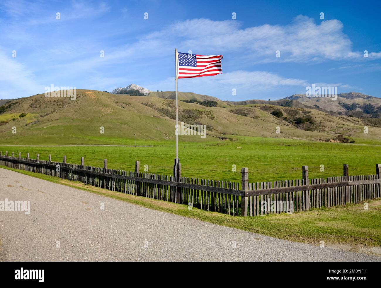 Patriotic scene of an American flag flying above a fence around a green ...