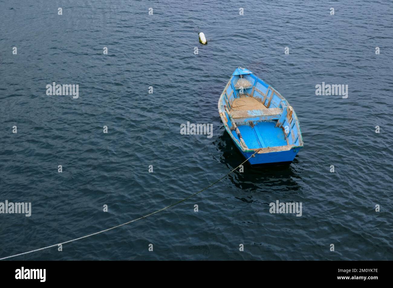 Weathered, bright blue rowboat in peeling paint anchored at sea Stock ...