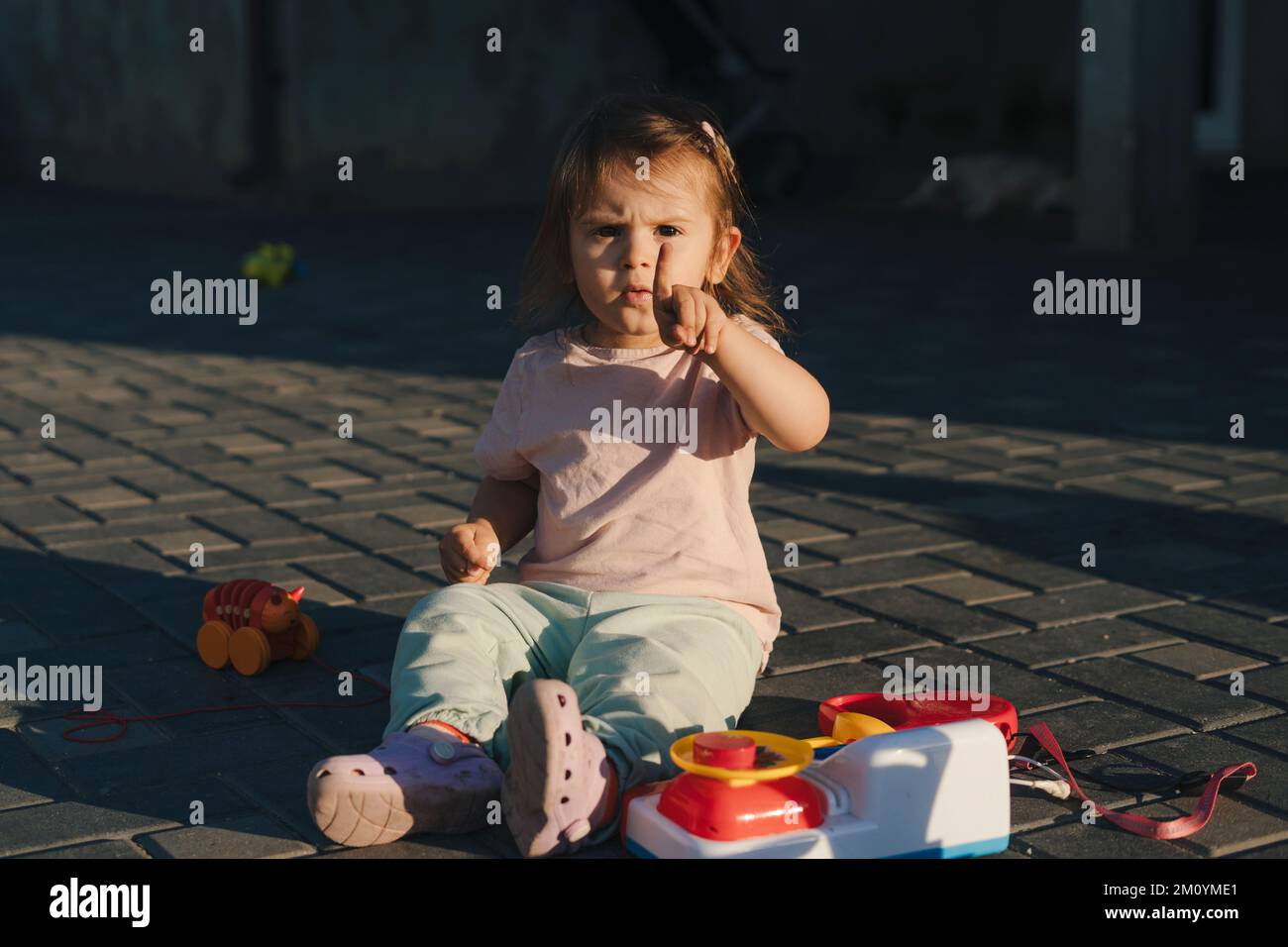 Concentrated baby girl standing outside in the yard of the house and ...