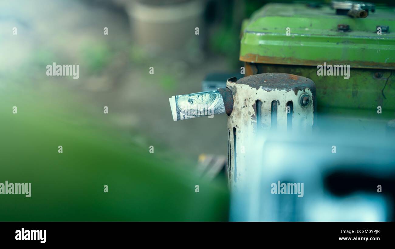 A hundred dollar bill is inserted into the muffler of a tractor exhaust ...