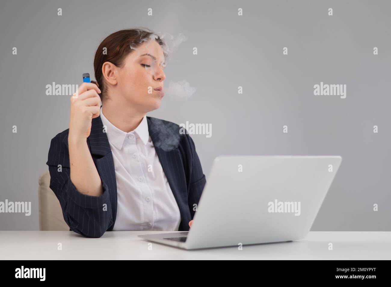 Business woman smoking a disposable vape while sitting at her desk ...