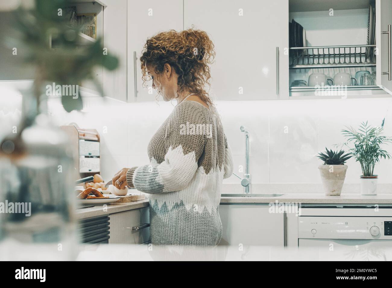 Side real view of woman cooking at home in the white minimal modern ...