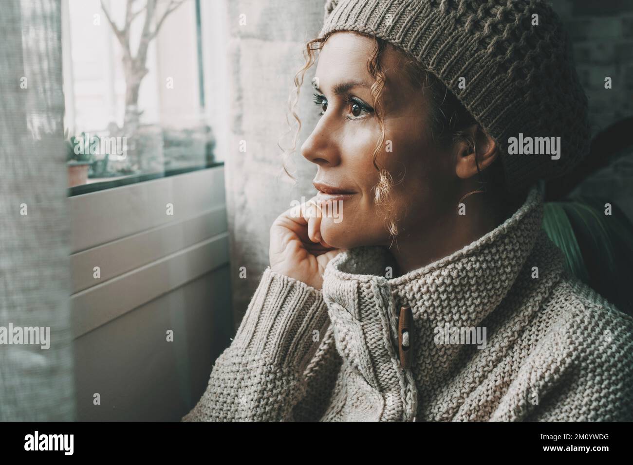 Side portrait of serene female looking outside the window at home in ...