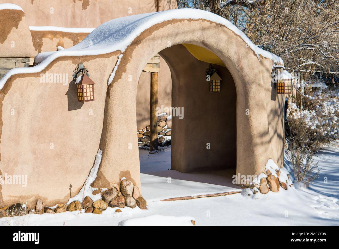 Snowy winter scene of a snow-covered adobe wall with an arched entrance ...