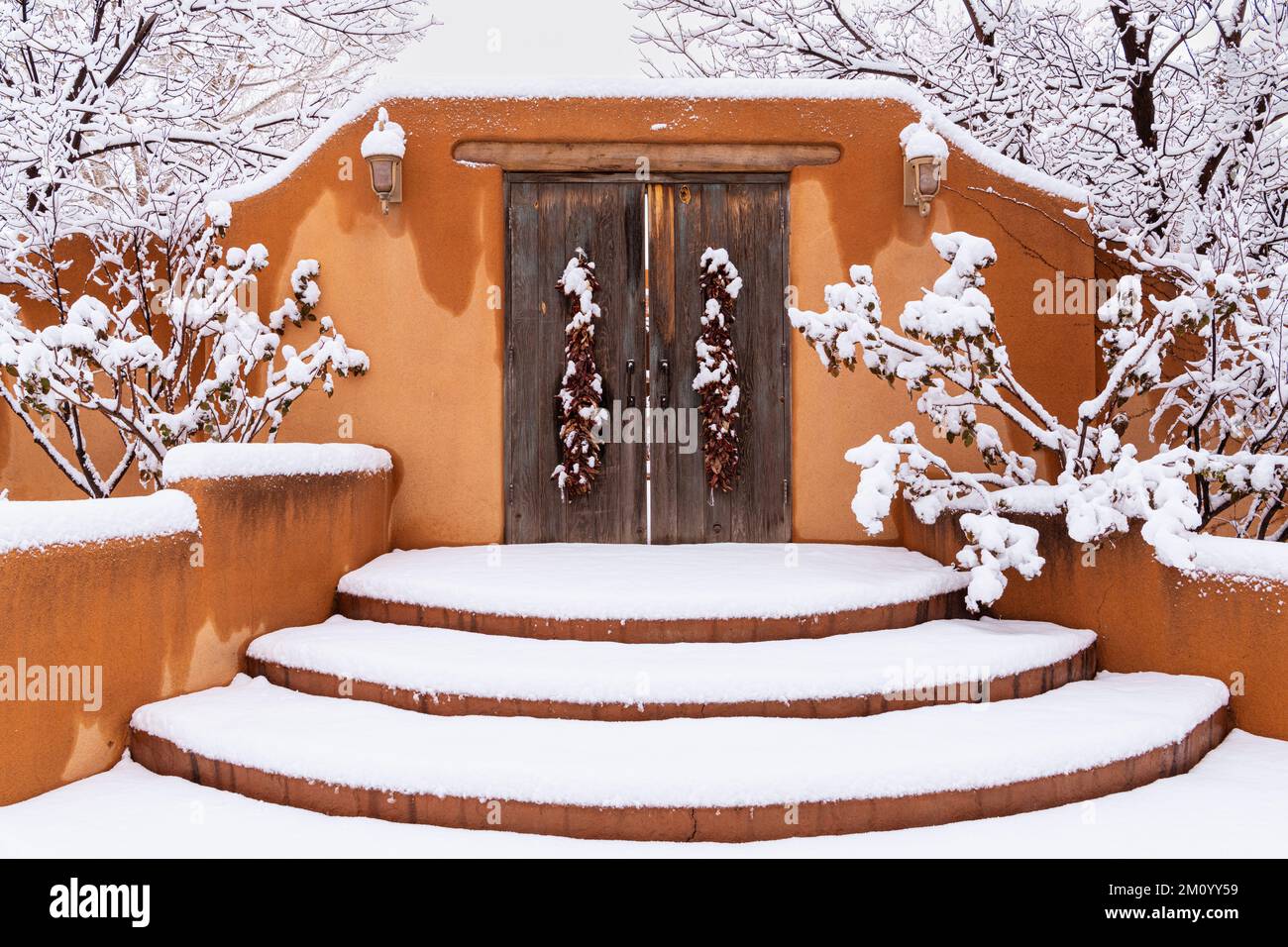 Winter scene of snow-covered adobe wall with rustic wood doors and ...