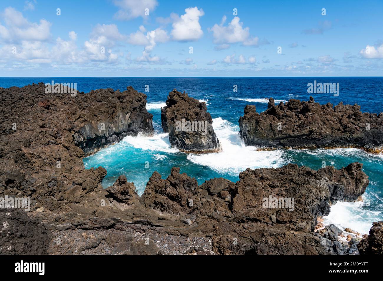 Cove with clear blue water beneath volcanic cliffs and rocks along the ...