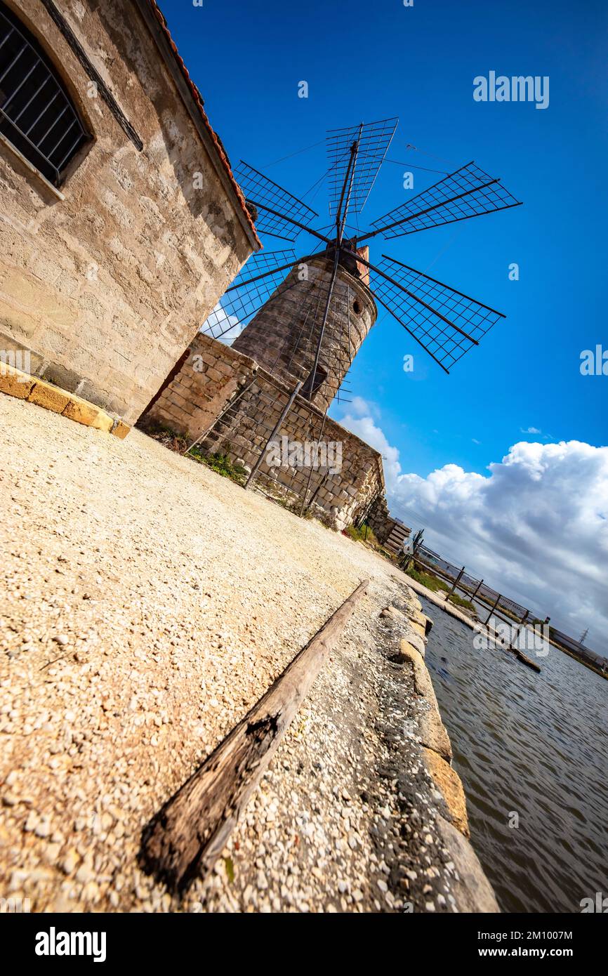 A vertical view of an old windmill by the water at the Trapani salt ...
