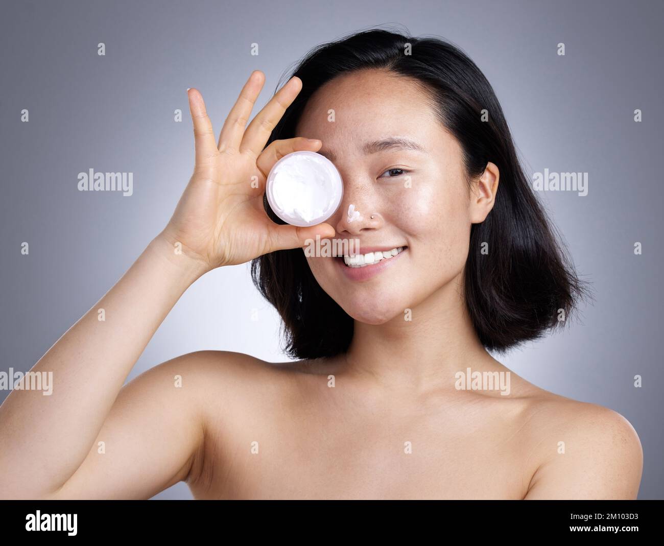 Eye love my moisturiser. a young woman applying lotion against a grey ...