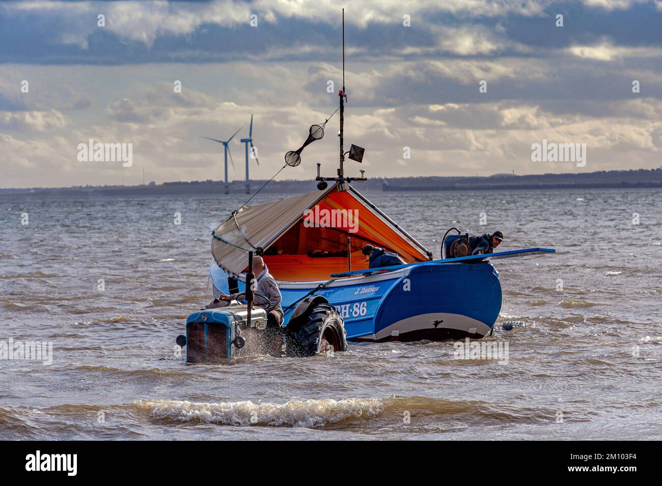 Tradditional Coble fishing boat being hauled out of the sea after a ...