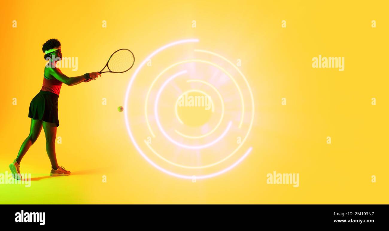 Side view of biracial female tennis player with racket by illuminated ...