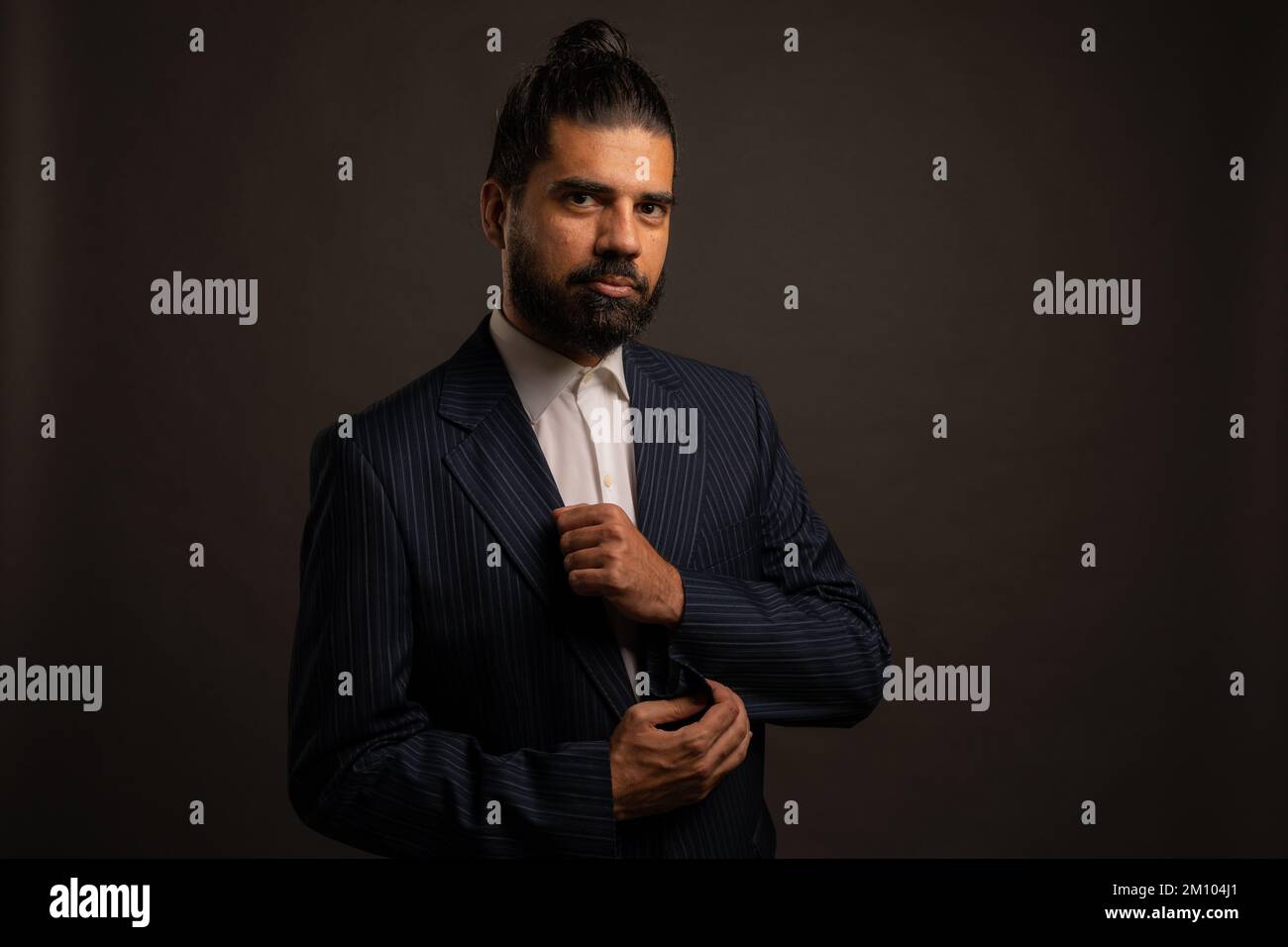 A Hispanic elegant male with long hair buttoning his suit isolated on ...