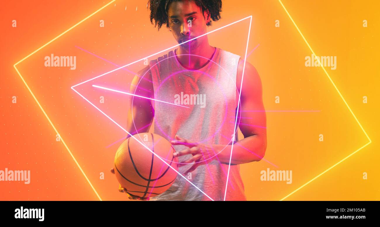 Serious biracial basketball player with ball standing over illuminated ...