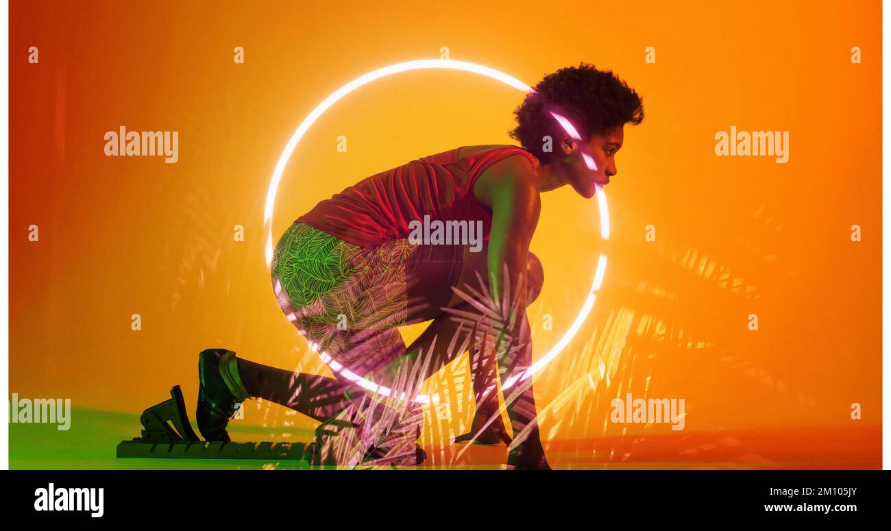 Biracial female athlete crouching at starting position by illuminated ...