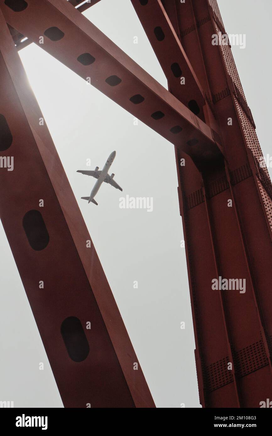 A vertical shot of the Golden Gate Bridge with an airplane flying above ...
