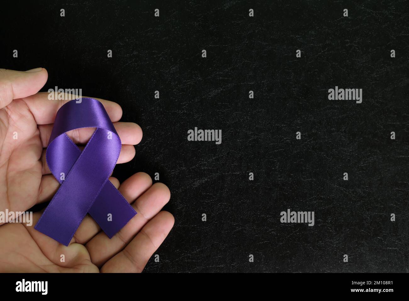 Human hand holding purple or violet ribbon color on dark black ...