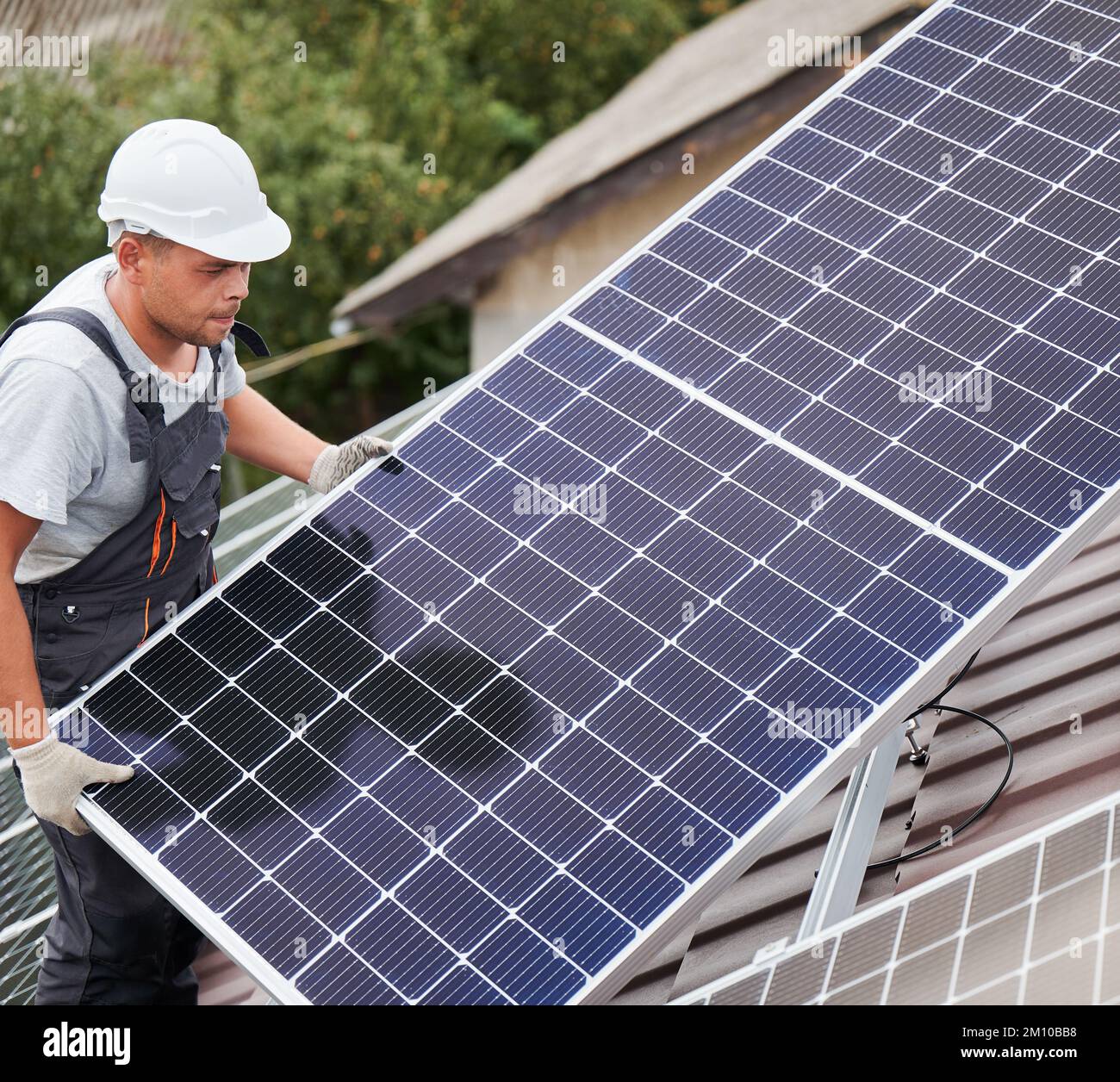 Man technician carrying photovoltaic solar moduls on roof of house. Electrician in helmet ...