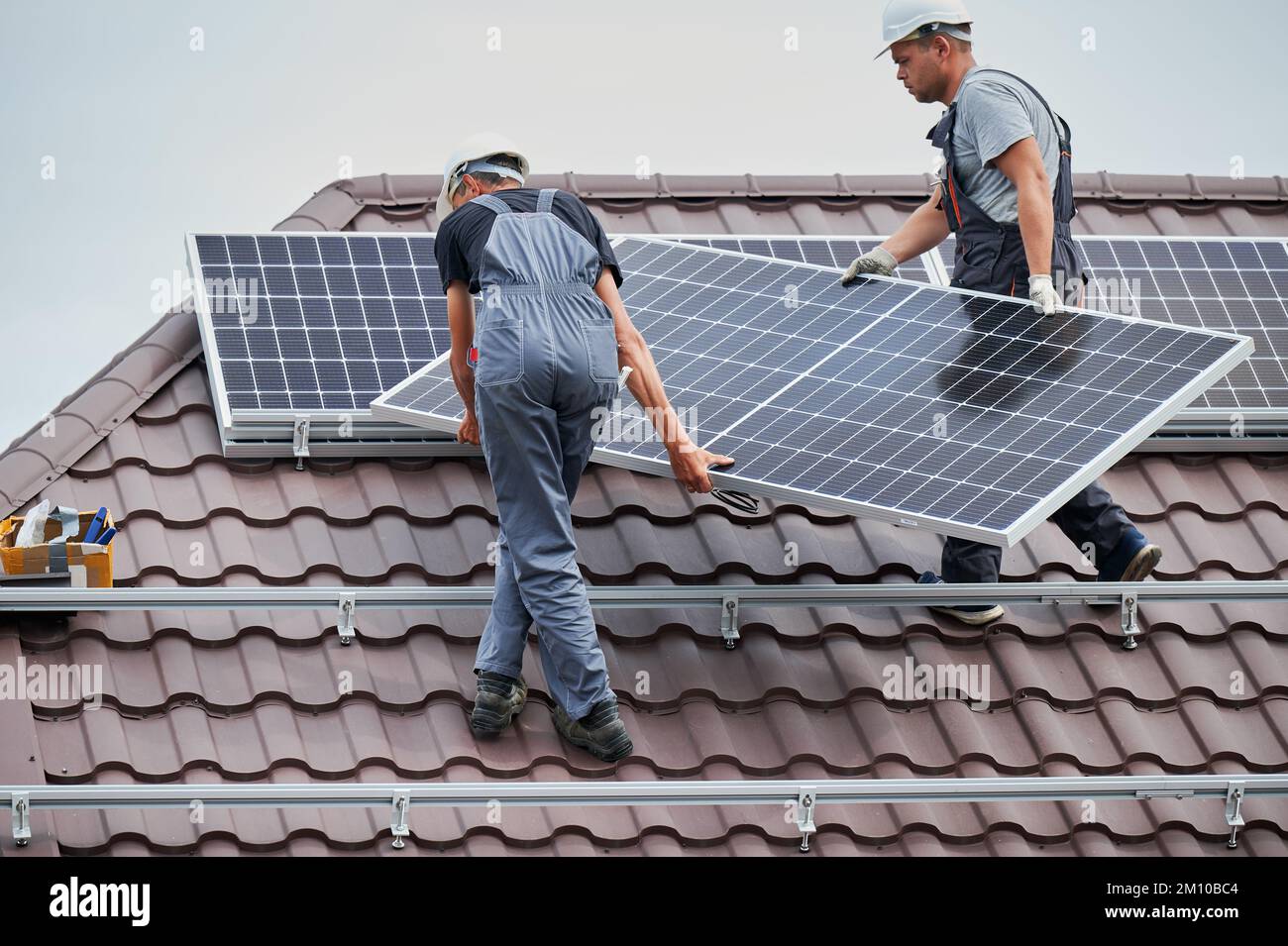 Men technicians carrying photovoltaic solar moduls on roof of house ...