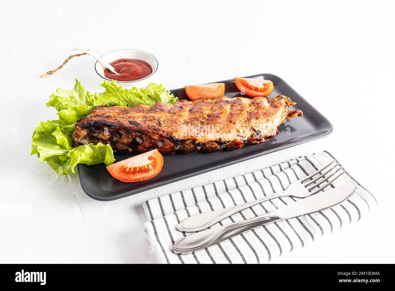 Grilled pork ribs are served on a rectangular dark ceramic plate with ...