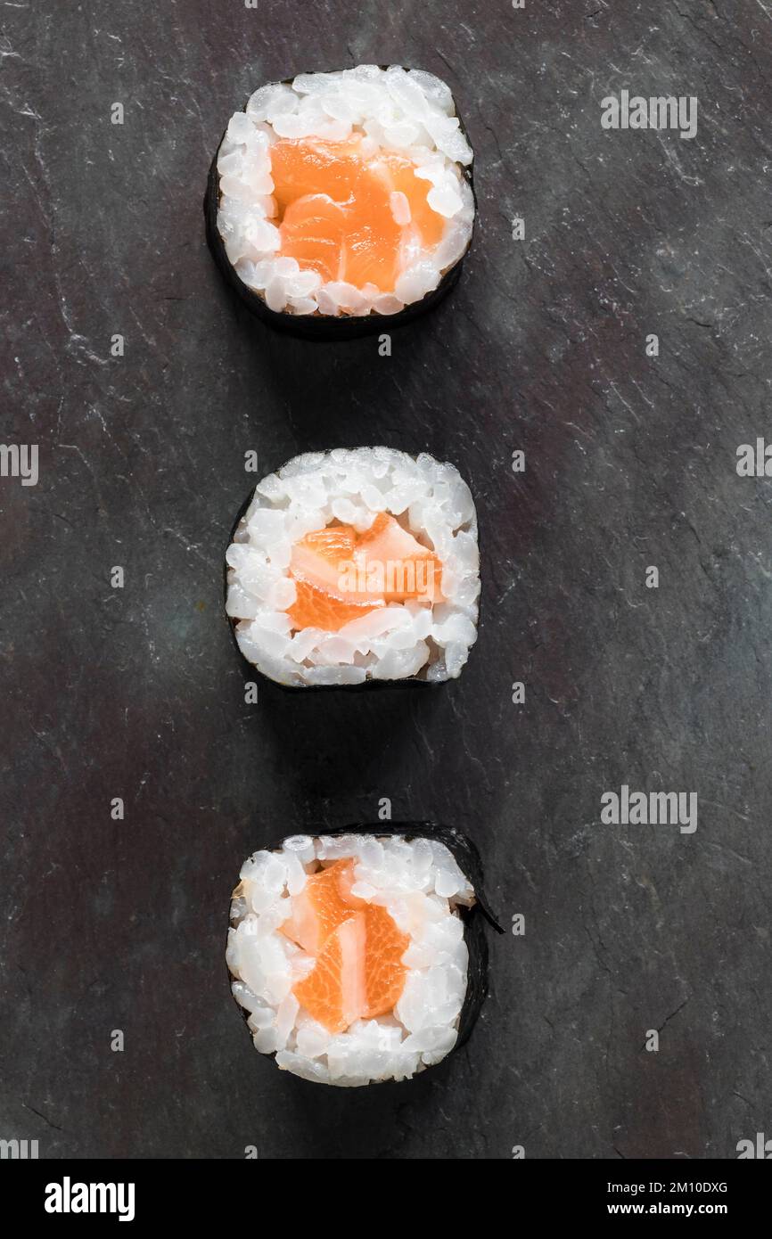 Macro top view of 3 salmon makis lined up on a black stone background ...