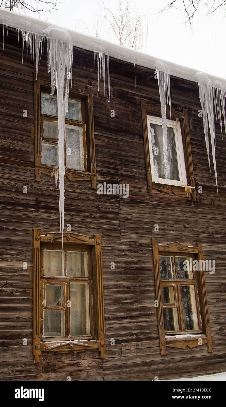 Growing, frozen icicles hang on the edge of the roof, winter or spring ...