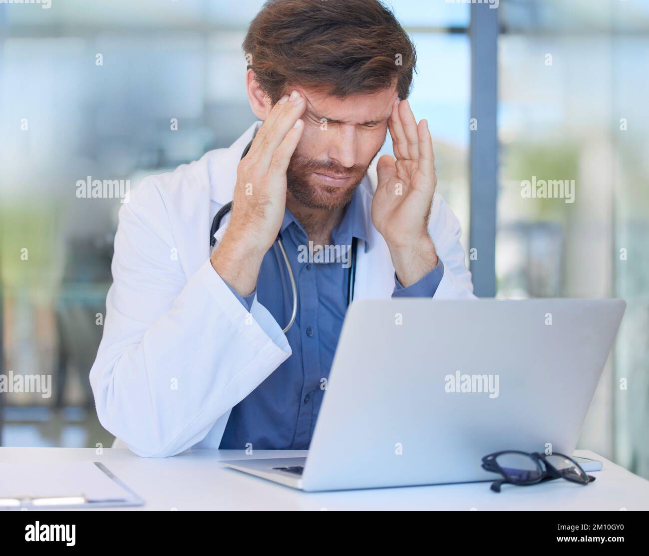 Headache, burnout and doctor in hospital office feeling pain or ...