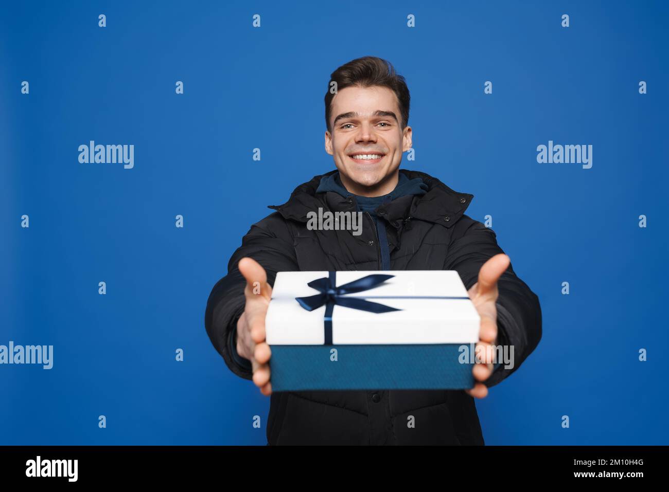 Young white man smiling while posing with gift box isolated over blue ...