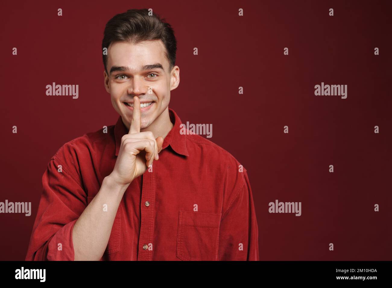 Young white man smiling and showing silence gesture at camera isolated ...