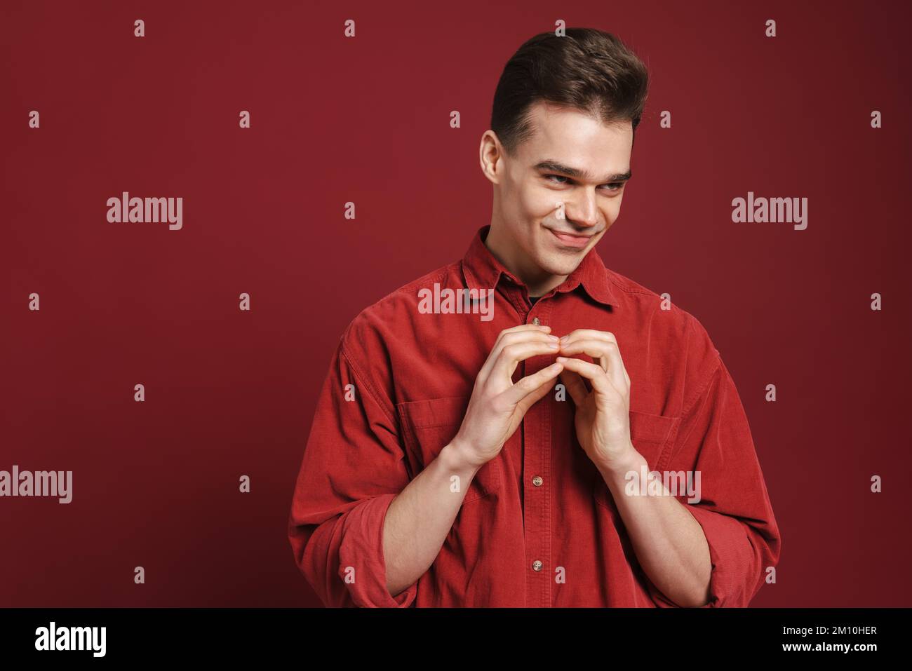 Young white man holding fingers together and smiling isolated over red ...