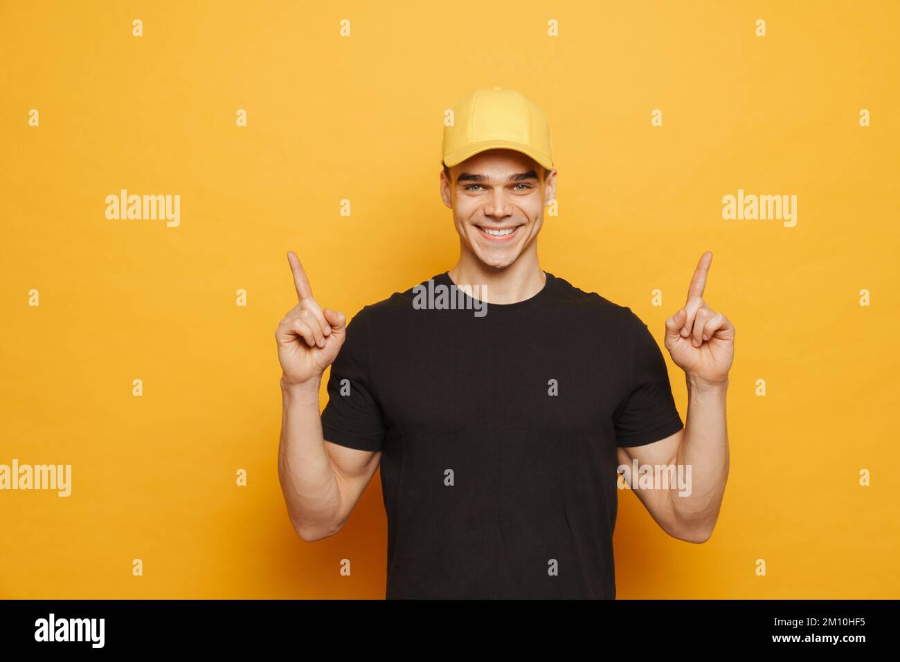 Young white man wearing cap smiling and pointing fingers upward ...