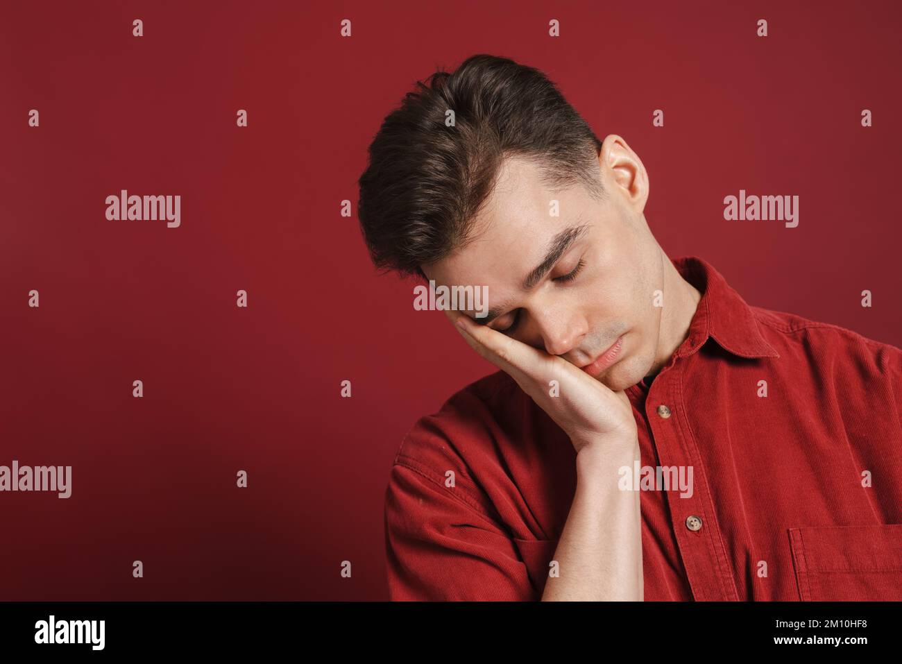 Young tired man propping up his head and slipping isolated over red ...