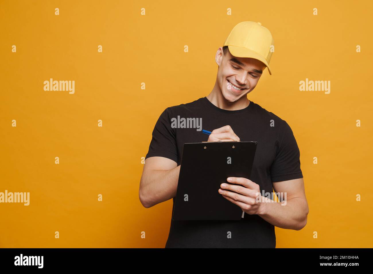 Young white man smiling while writing on clipboard isolated over yellow ...