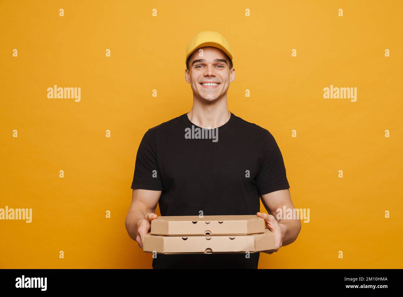 Young delivery man smiling while posing with pizza boxes isolated over ...