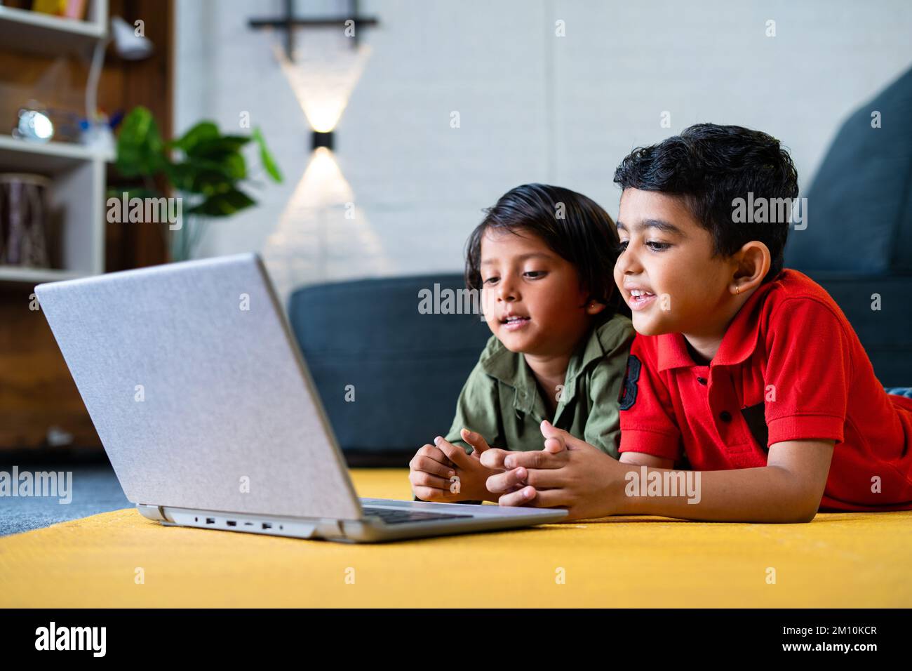 young kids watching videos on laptop while lying on floor at home ...