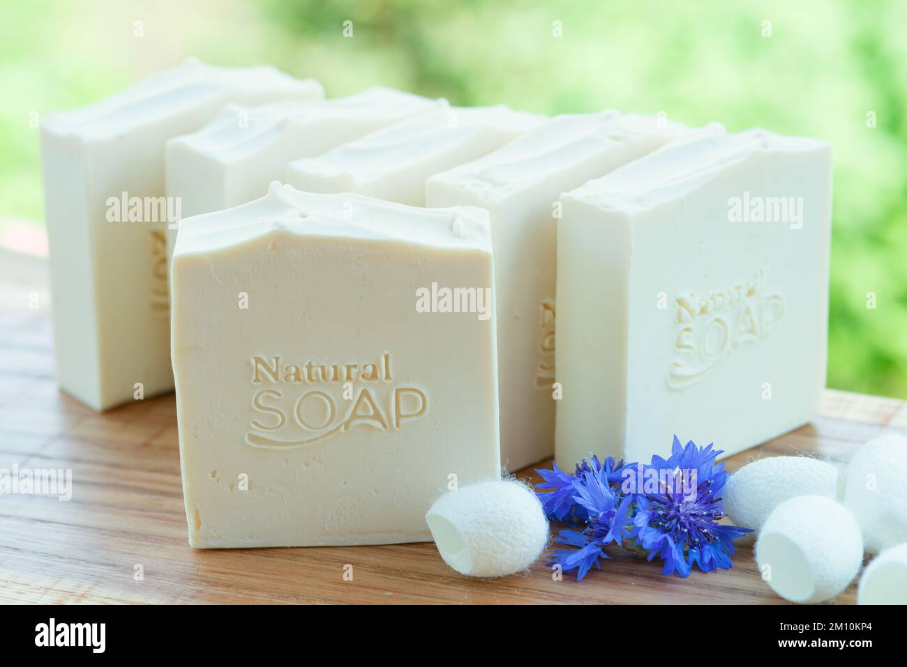 White handmade soap with blue flowers and silk cocoons on a green ...