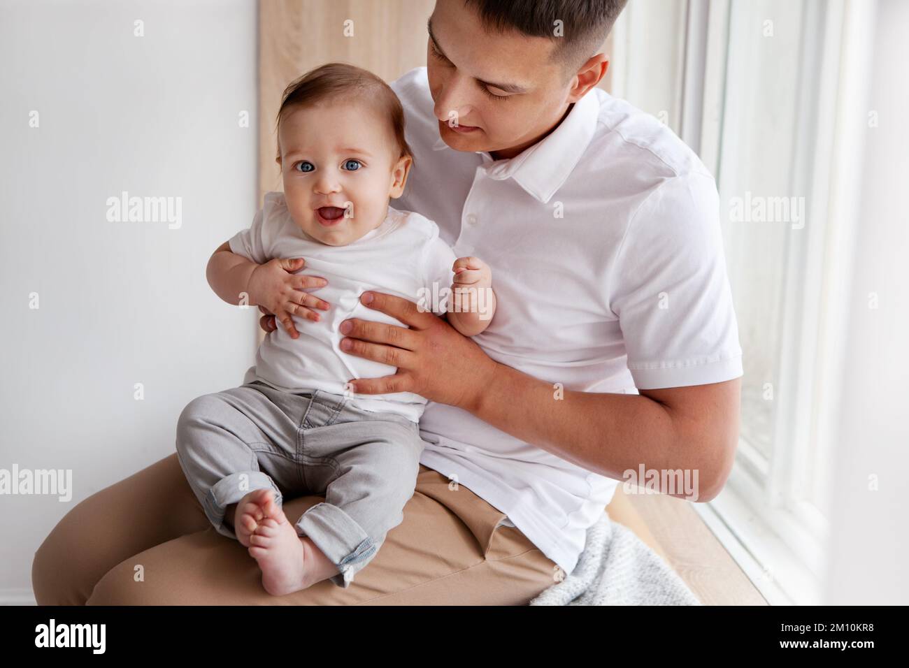 Close up small child sitting on dad lap, looking at camera and smiling ...