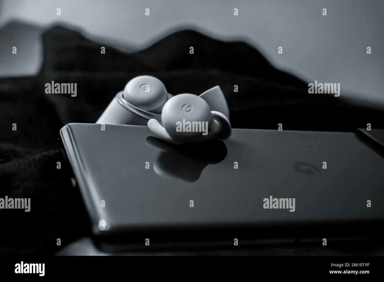 A grayscale shot Google Pixel Buds with a mobile device on black and ...