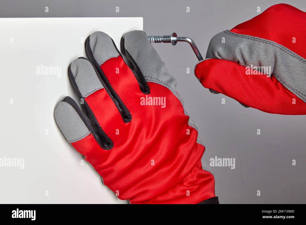 Furniture assembler in red gloves is screwing in a screw with a hex ...