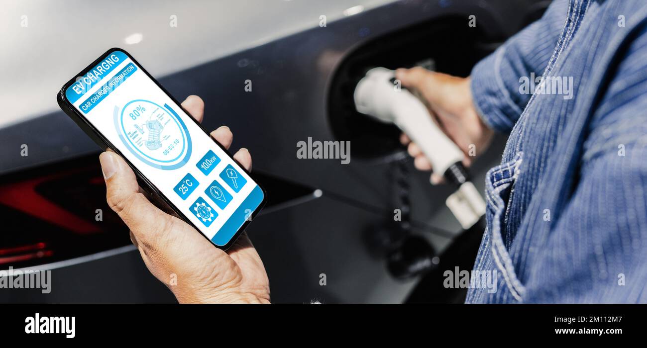 Man Charging Electric Vehicle With Cable Looking At App On Mobile Phone ...