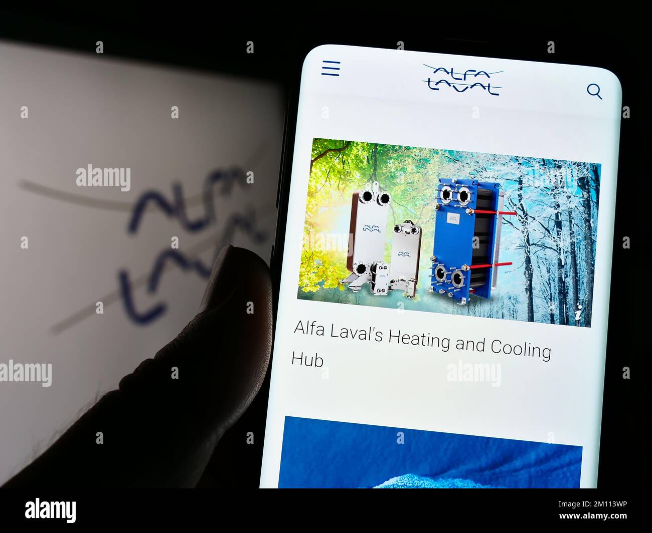 Person holding cellphone with webpage of Swedish company Alfa Laval AB on screen in front of ...
