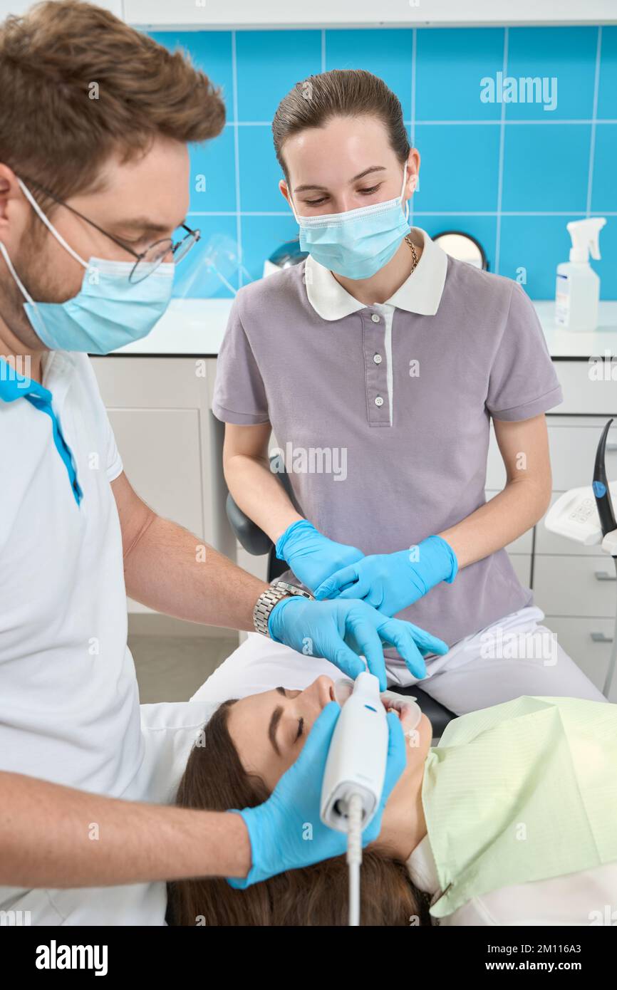 Doctor carrying out examination of client teeth with modern diagnostic ...