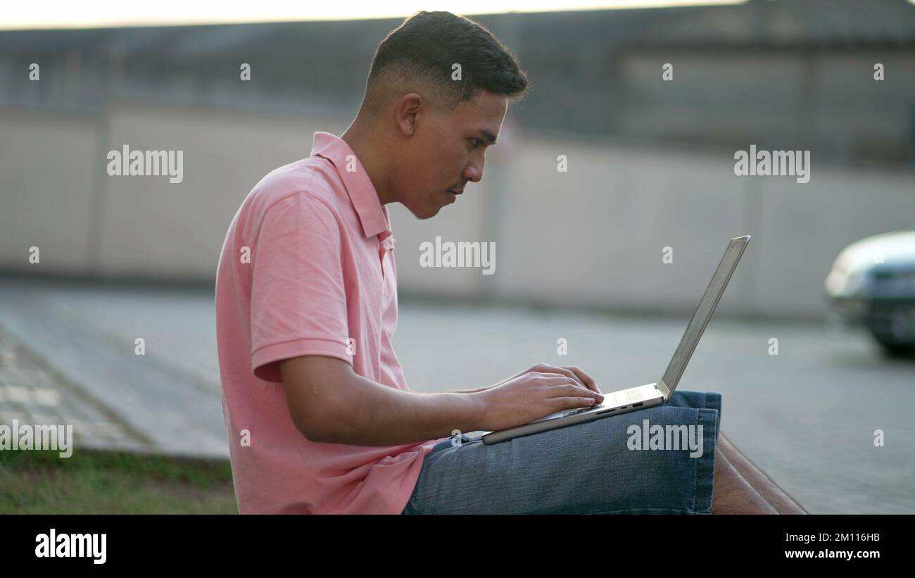 A young hispanic man opening laptop computer screen outside. Candid ...