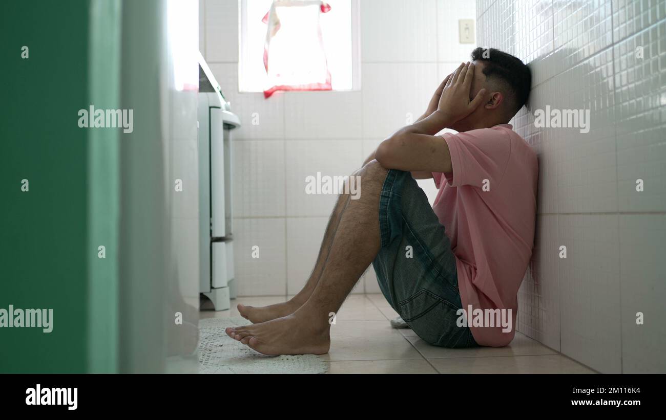 Depressed man sitting on floor. Sad unhappy person holding his forehead ...