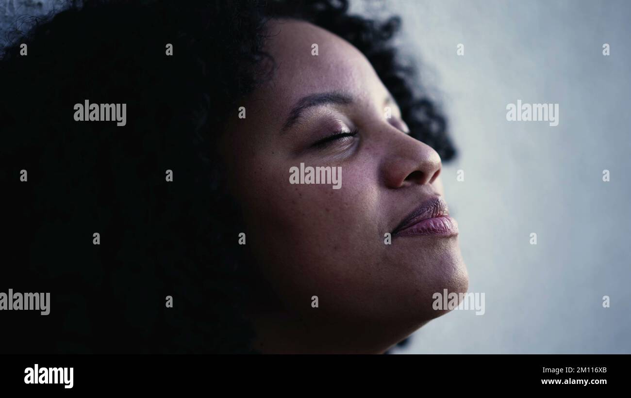 One hopeful meditative young black woman with eyes closed in ...