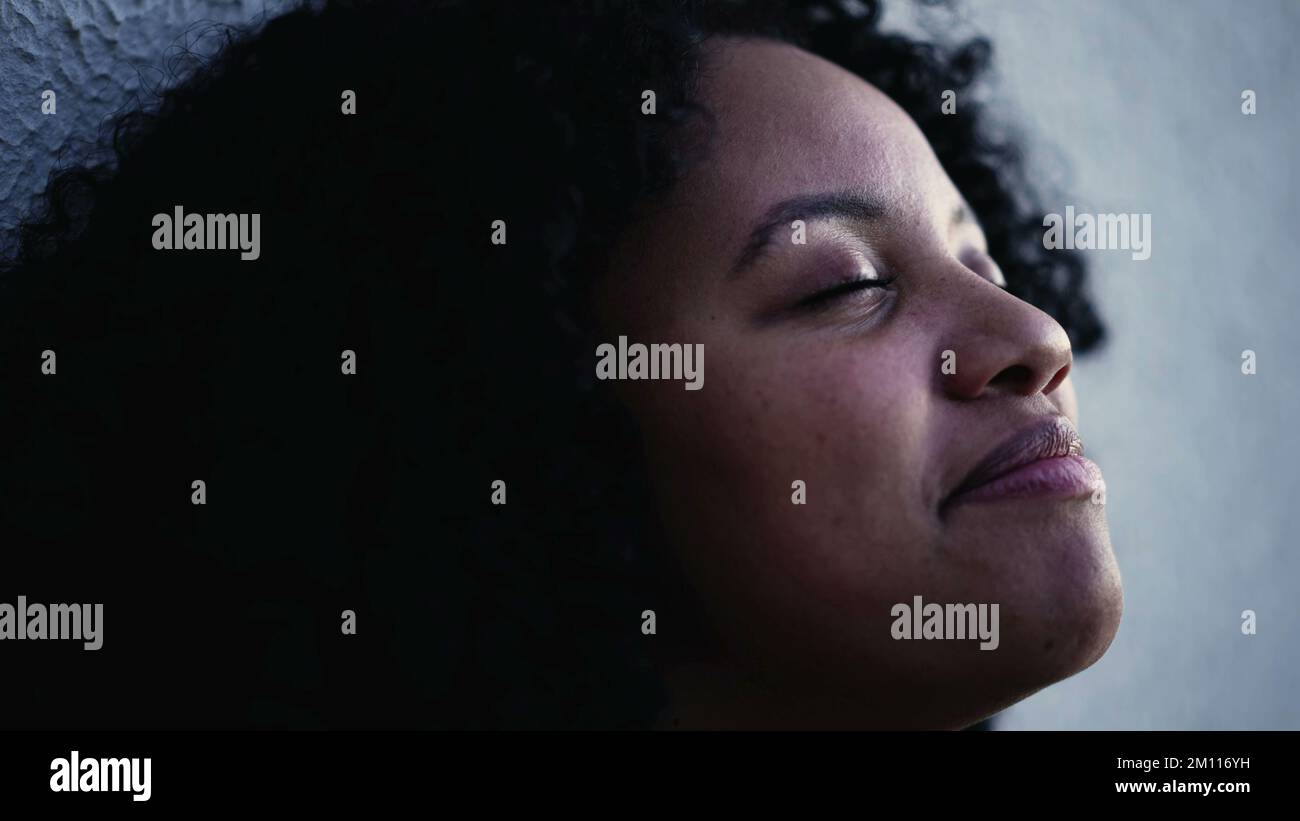 One hopeful meditative young black woman with eyes closed in ...